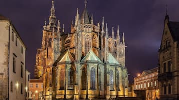 Uma catedral gótica com torres elaboradas e vitrais coloridos, cercada por edifícios históricos.