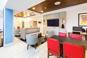 Quarto de hotel moderno com sofá, cadeiras, mesa de jantar e televisão.