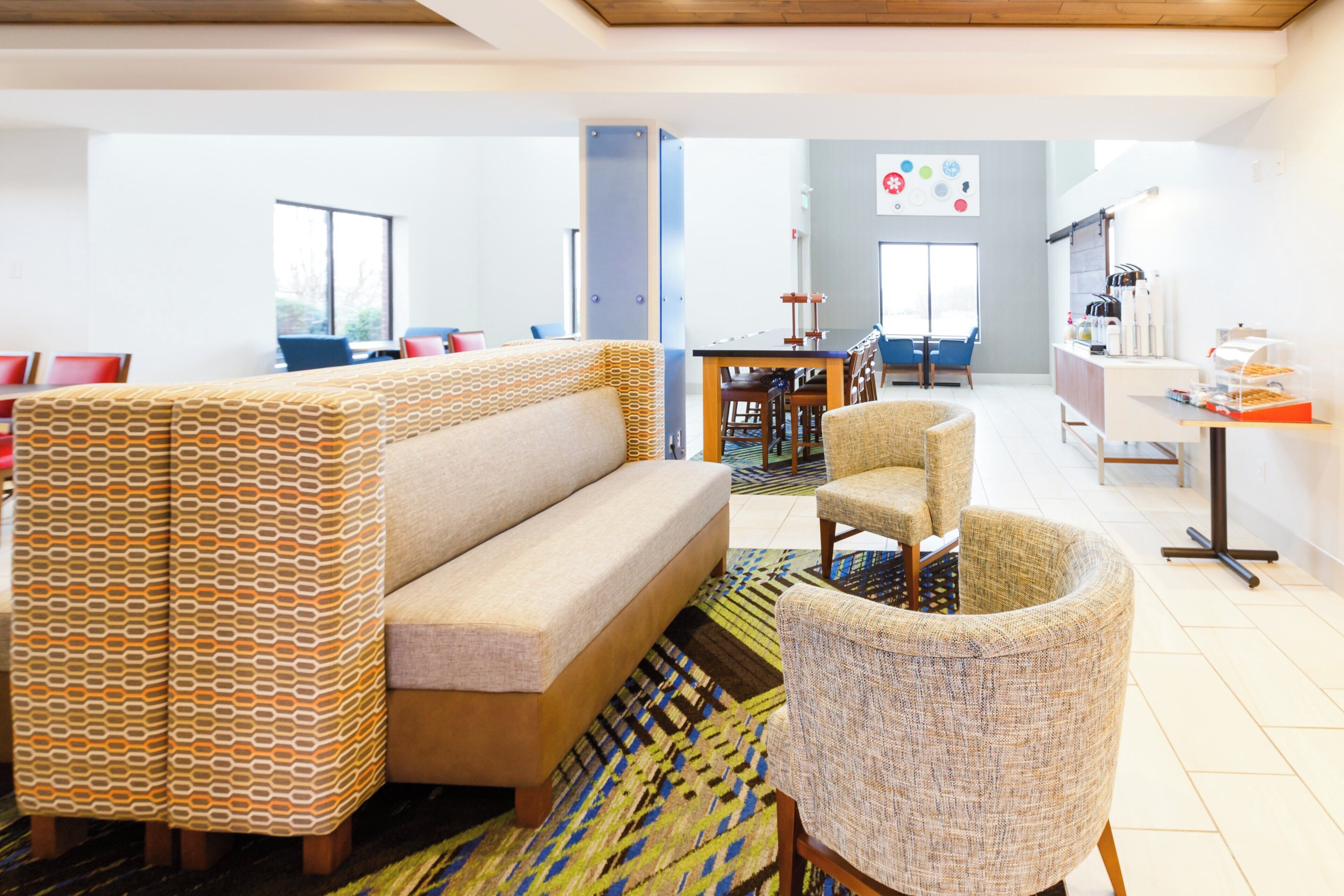 Um hall de hotel moderno com um sofá, poltronas, área de refeições e um espaço com cozinha.
