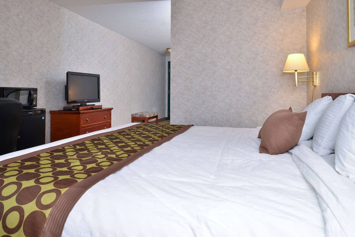 Quarto de hotel com cama, televisão, secretária e computador, além de uma luminária.