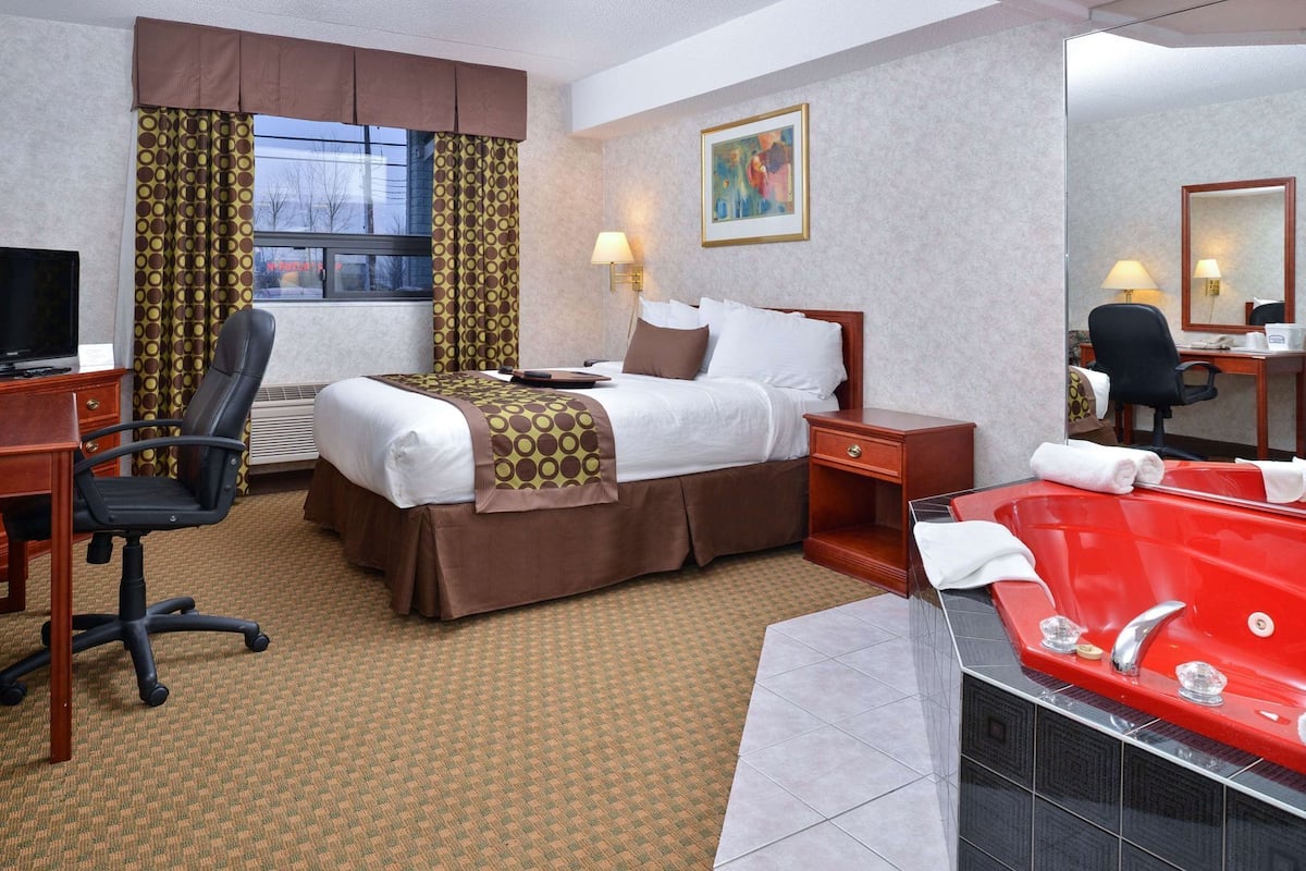 Quarto de hotel com cama, escrivaninha, cadeira e uma banheira de hidromassagem vermelha.