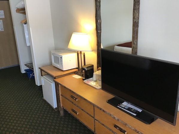 Quarto de hotel com escrivaninha de madeira, televisão de tela plana, micro-ondas, luminária e pequena geladeira.
