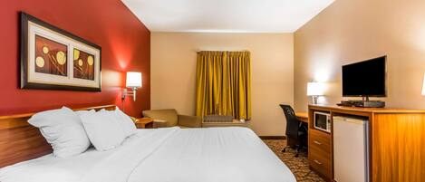 Quarto de hotel com uma cama grande, uma escrivaninha com computador, televisão e minibar.
