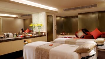 Um quarto de spa com duas camas, uma toucador com espelho, velas e um arranjo floral.