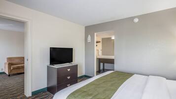 Quarto de hotel com cama, televisão sobre uma cômoda, uma cadeira e banheiro visível por uma porta aberta.