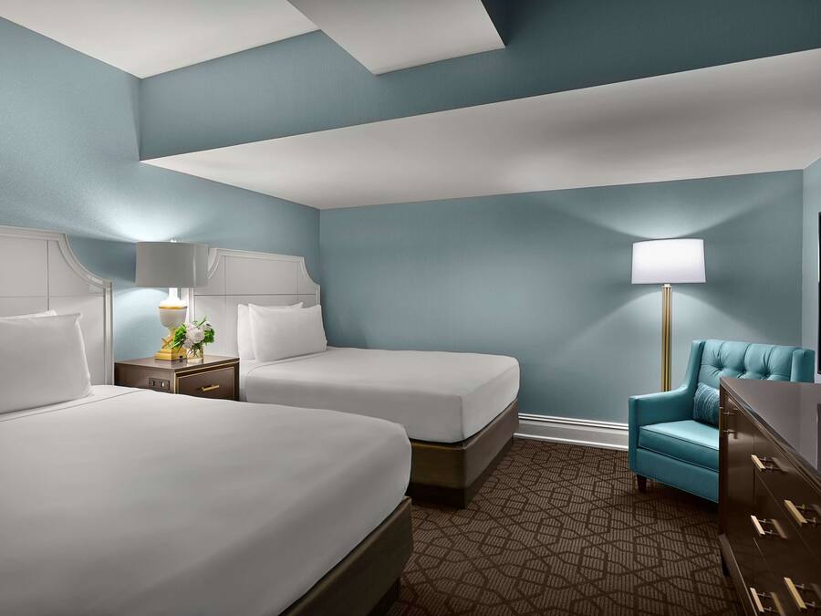 Quarto de hotel com duas camas, uma televisão, uma escrivaninha e uma cadeira.