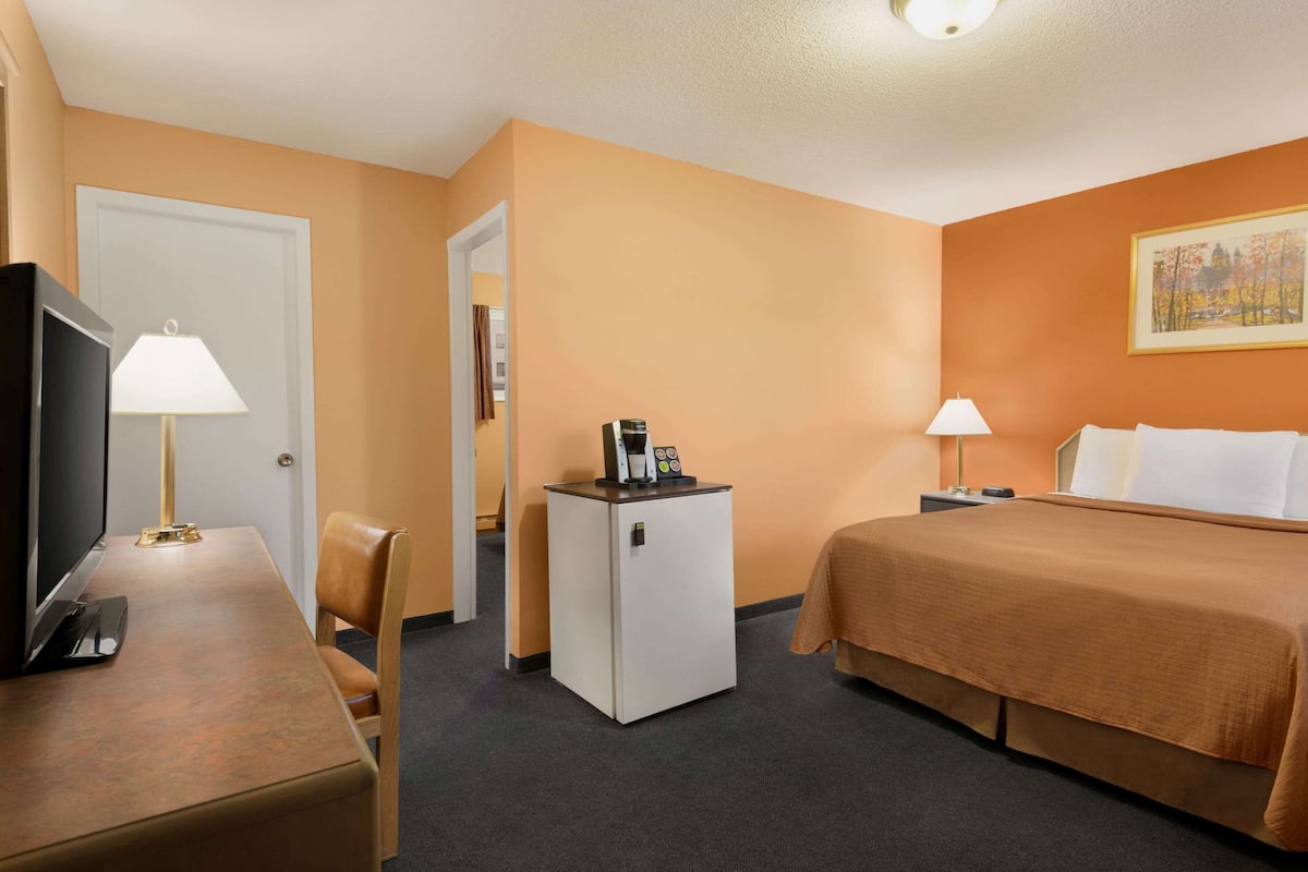 Quarto de hotel com cama, escrivaninha, computador, pequeno frigorífico e televisão.