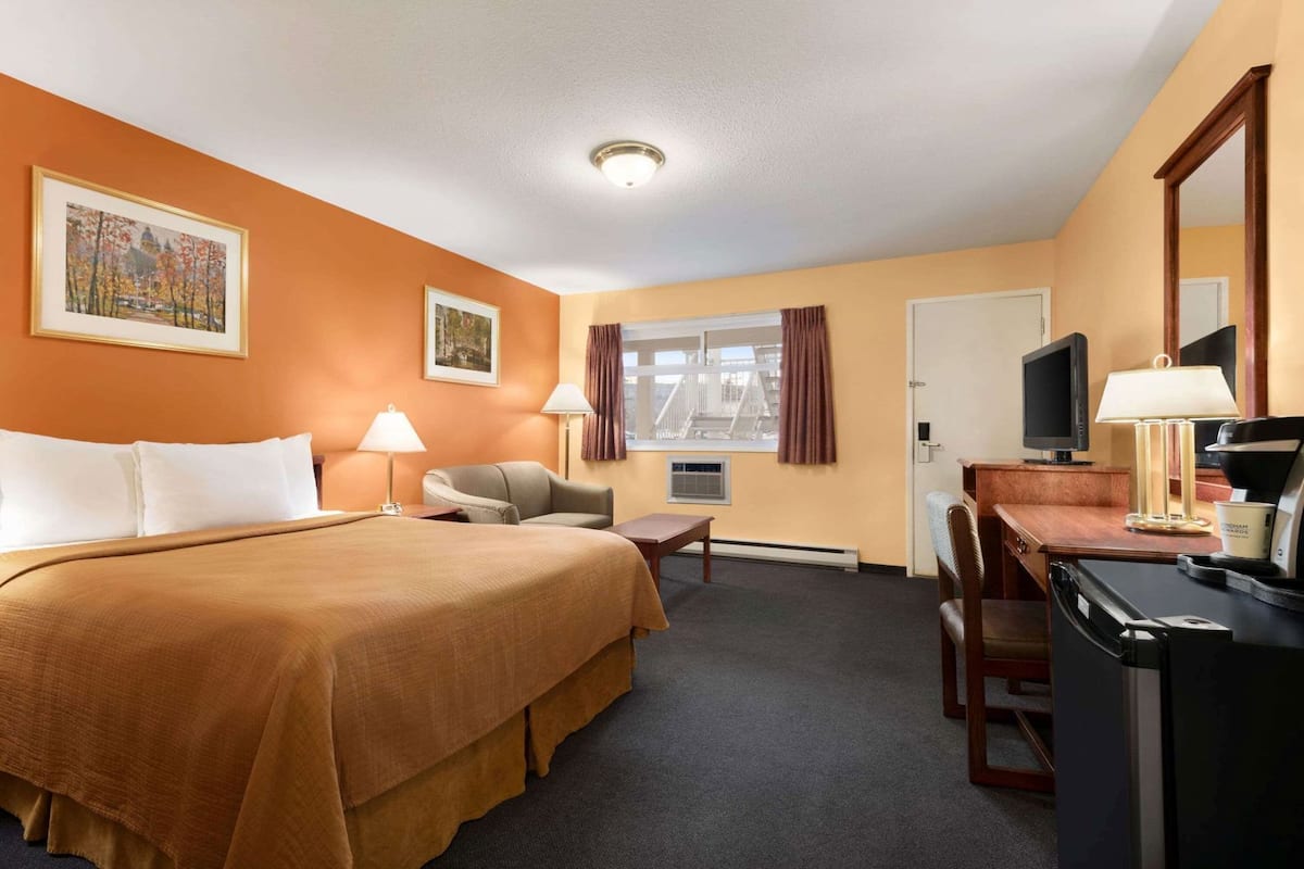 Quarto de hotel com uma cama grande, duas mesas de cabeceira com luminárias, uma escrivaninha com cadeira, televisão e cafeteira.
