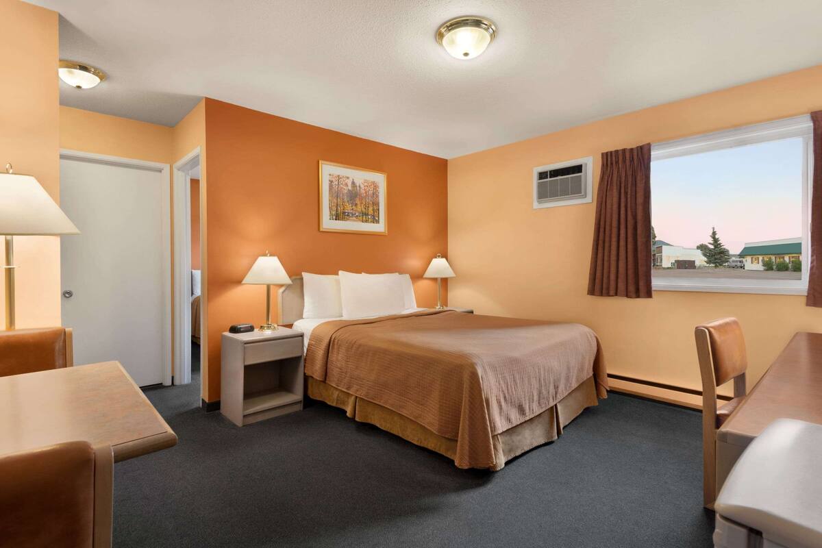 Quarto de hotel com uma cama, duas mesas de cabeceira com luminárias, uma escrivaninha e uma cadeira.