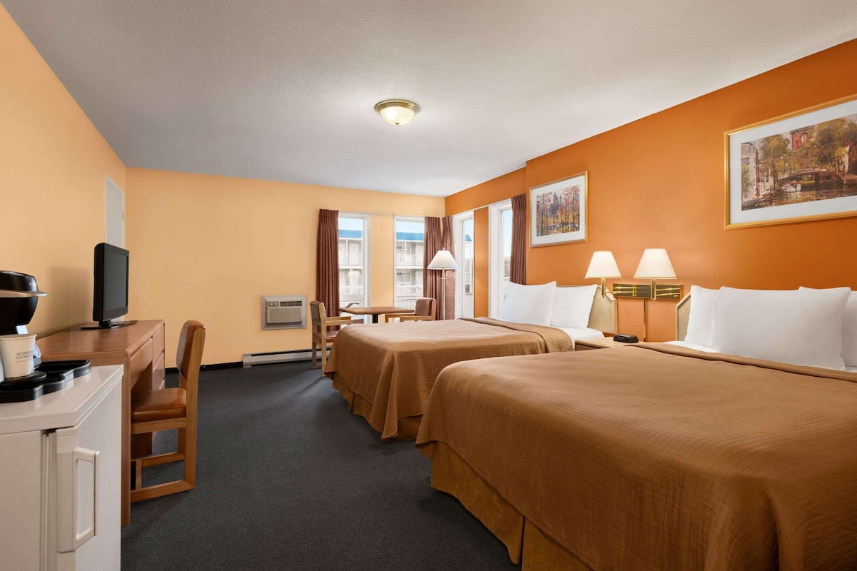 Quarto de hotel com duas camas, uma mesa com computador, uma cadeira, televisão e uma janela com cortinas.