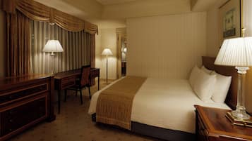Quarto de hotel com uma cama, uma escrivaninha, uma cadeira e duas luminárias.
