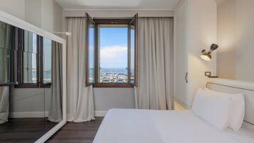 Quarto de hotel com uma cama grande, um espelho, uma janela com vista para uma marina e um candeeiro fixado na parede.