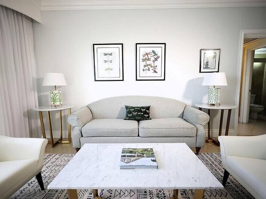 Uma sala de estar moderna com um sofá bege, duas mesas laterais com luminárias, uma mesa de centro com um livro e gravuras botânicas emolduradas na parede.