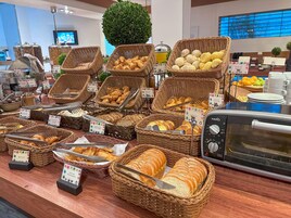 Buffet com diversos pães e doces expostos em cestas de vime, máquina de café e torradeira.
