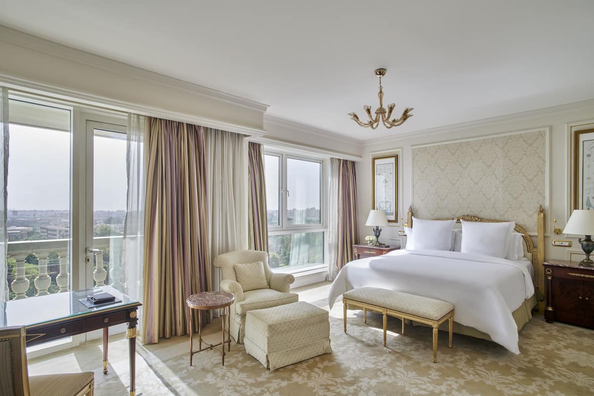 Quarto de hotel com uma cama grande, uma escrivaninha, uma cadeira e vista para a cidade através de amplas janelas.
