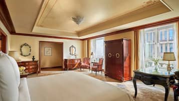 Quarto de hotel espaçoso com uma cama grande, um guarda-roupa de madeira, uma escrivaninha com uma lâmpada e vista da cidade através de grandes janelas.