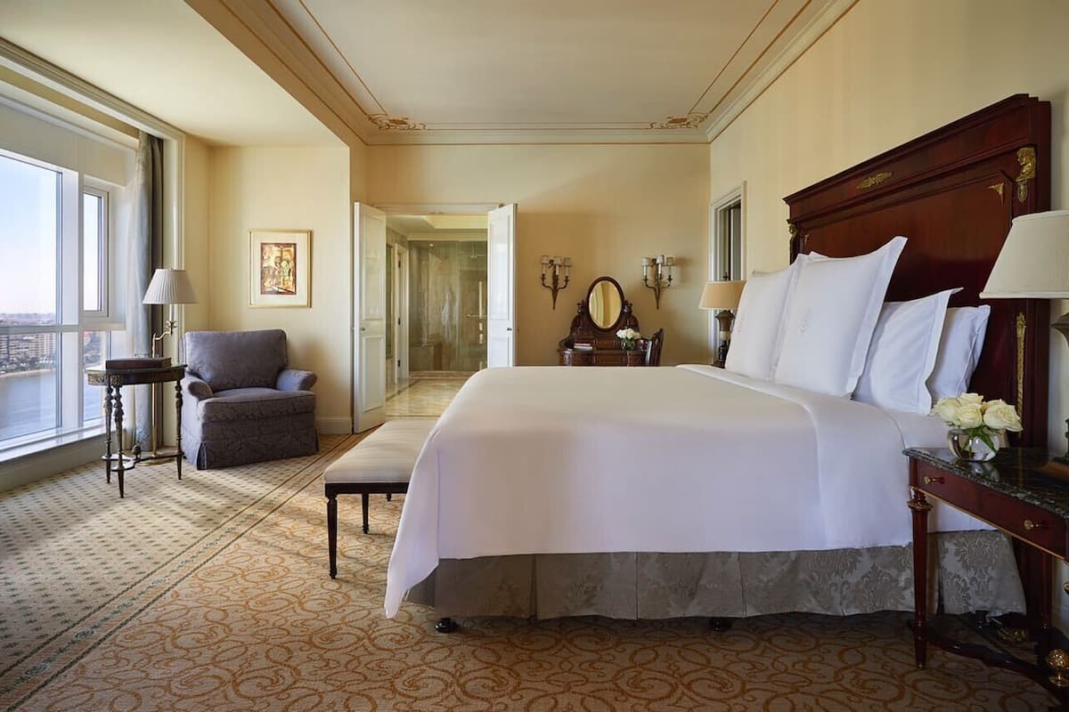 Quarto de hotel com uma cama grande, uma cadeira, uma mesa e vista para a cidade.