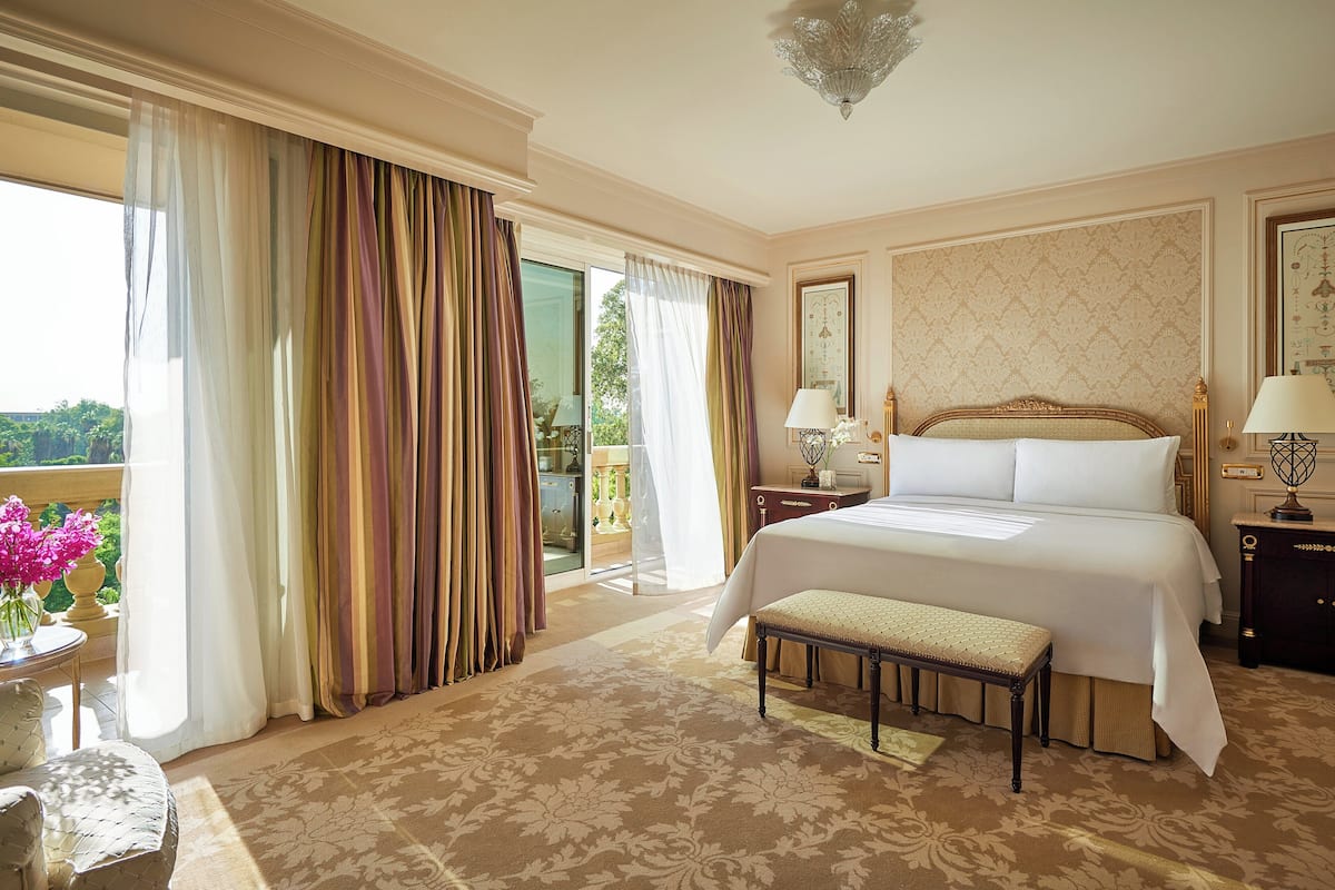Quarto de hotel com uma cama grande, um banco, uma mesa de cabeceira e vista para o exterior.