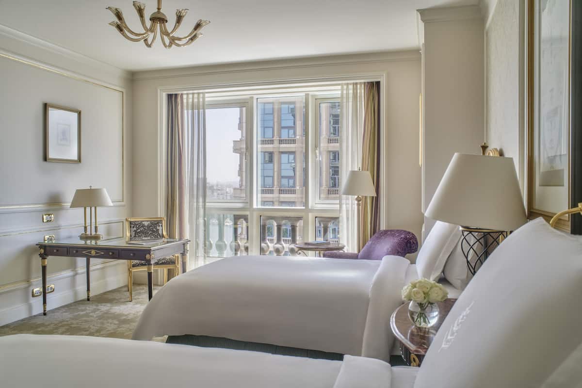 Quarto de hotel com duas camas, uma escrivaninha e uma cadeira.