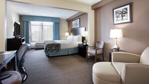 Quarto de hotel com cama, escrivaninha, cadeira e televisão.