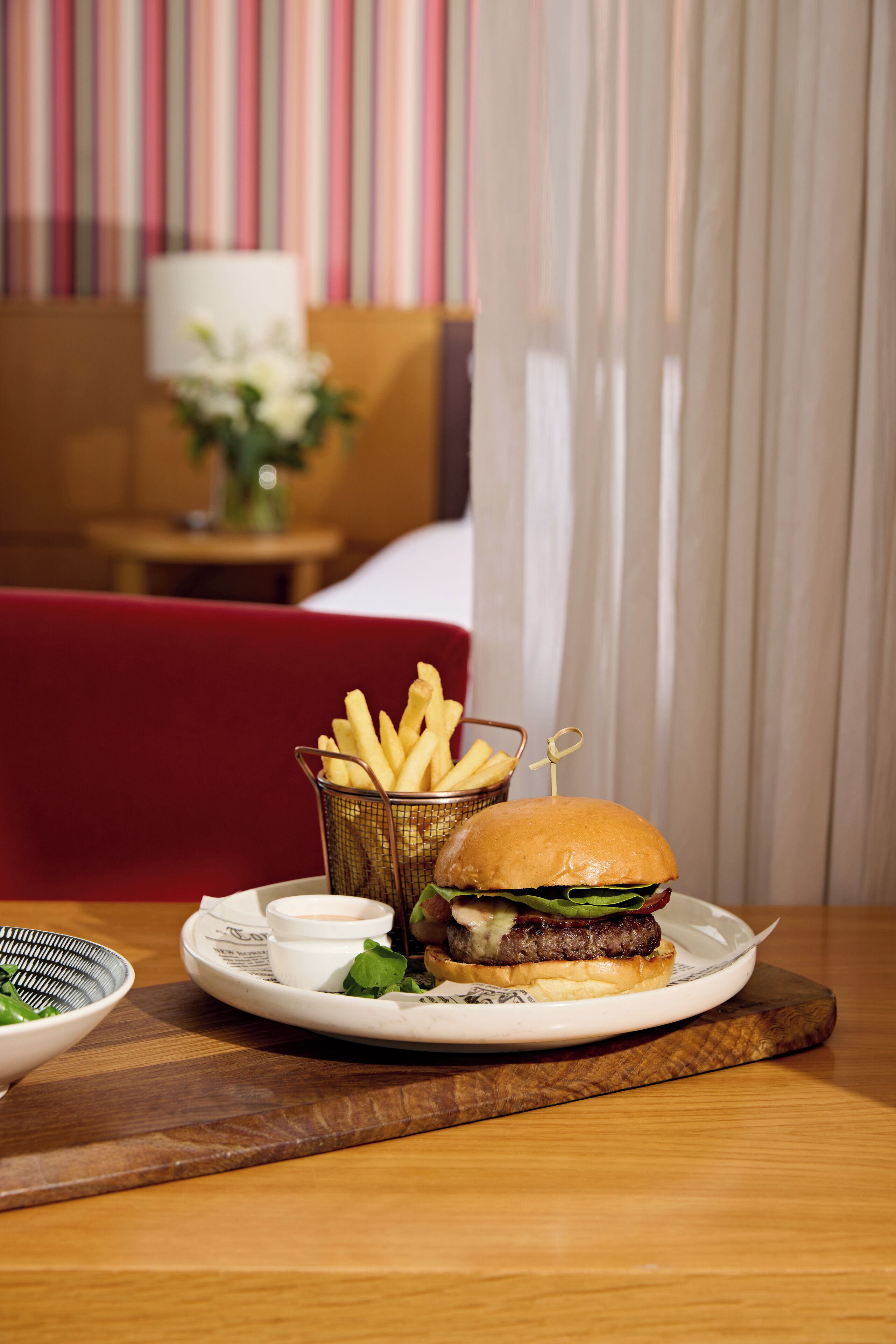 Uma mesa de jantar com um prato de comida, incluindo um hambúrguer e batatas fritas, em um quarto de hotel.