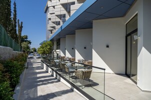 Um edifício moderno com área de estar coberta ao ar livre, guarda-corpo de vidro e vista desimpedida da rua.