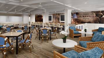 Um restaurante com mesas e cadeiras redondas, área de bar e parede com pôster vintage.