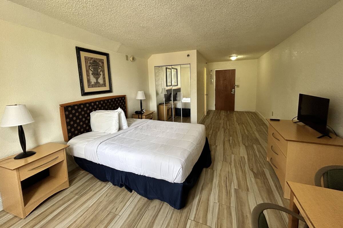 Quarto de hotel com cama grande, mesas de cabeceira, televisão e espelho.