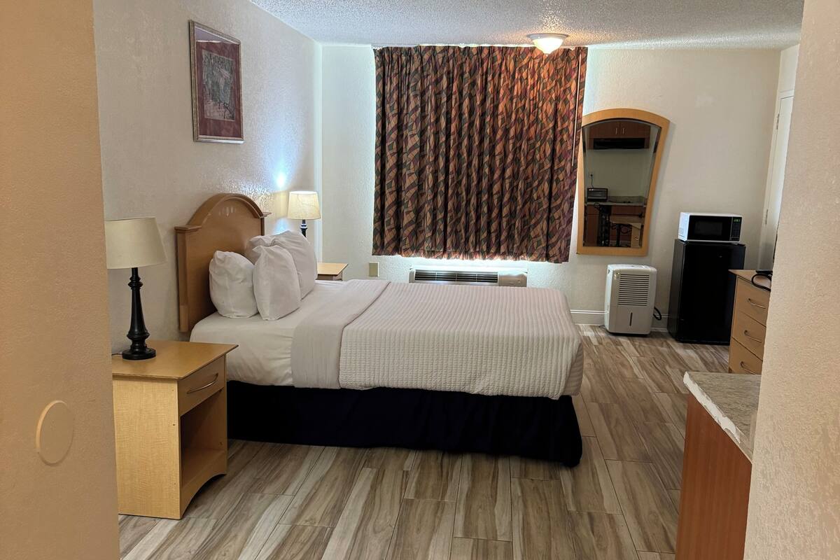 Quarto de hotel com cama, mesas de cabeceira, espelho, micro-ondas e frigorífico.
