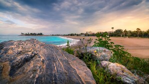 Linha costeira rochosa com uma praia e vista distante de um horizonte urbano.