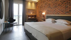 Quarto de hotel moderno com uma cama grande, uma mesinha, uma cadeira, um criado-mudo e uma parede com padrão de tijolos.