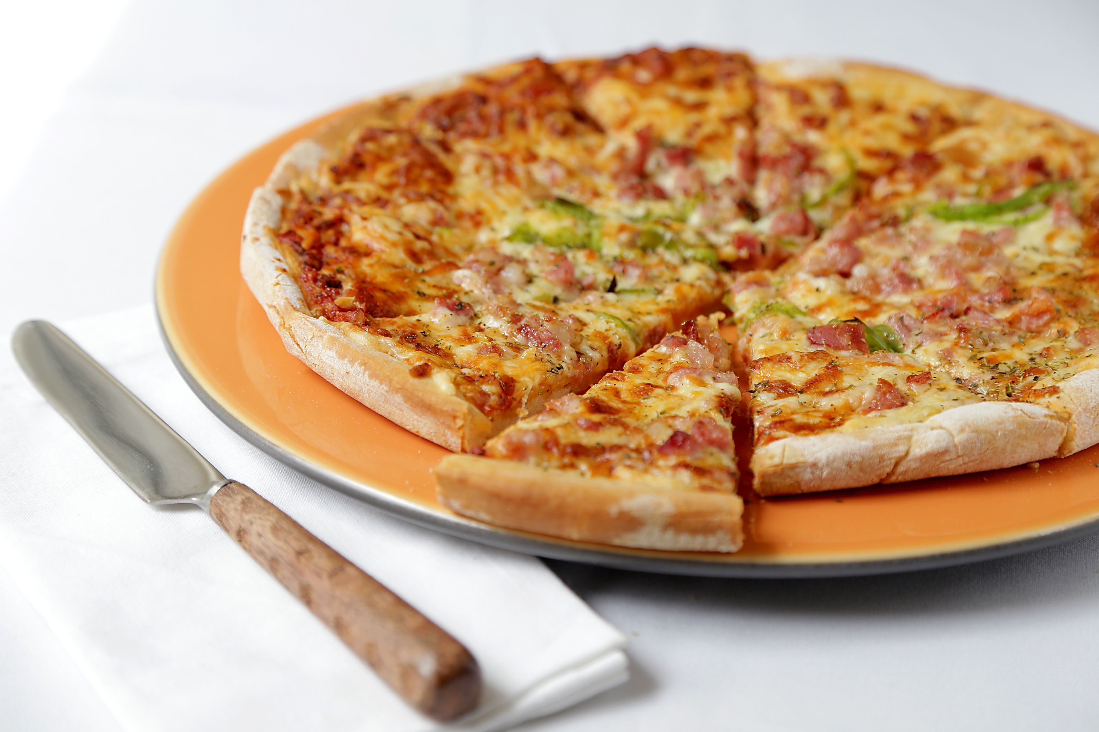 Pizza em um prato com uma faca e guardanapo ao lado.