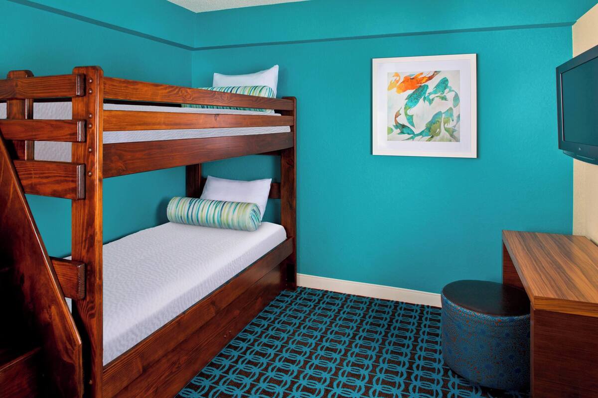 Quarto com beliche, parede azul-turquesa, uma obra de arte emoldurada e televisão.