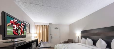Quarto de hotel com televisão em uma escrivaninha, cama com colcha estampada, escrivaninha com cadeira e uma porta.