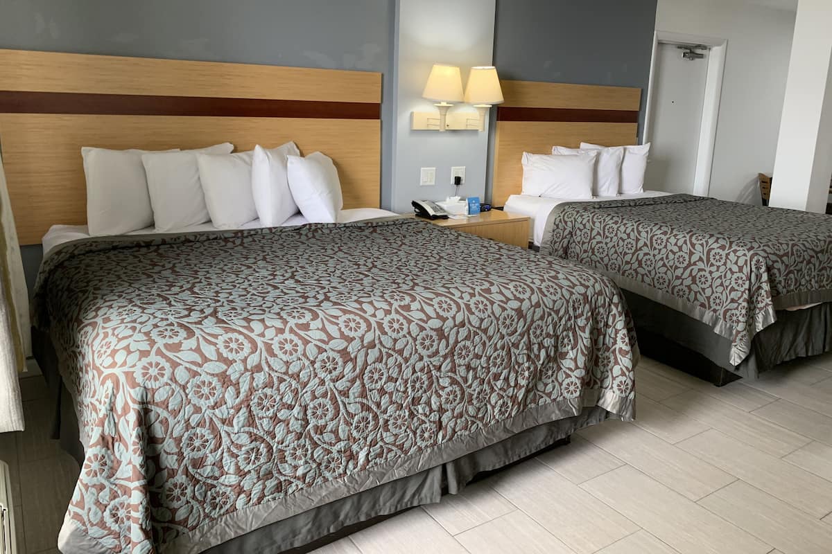 Quarto de hotel com duas camas, cada uma com colcha estampada de flores, cabeceira de madeira e mesa de cabeceira com abajur.