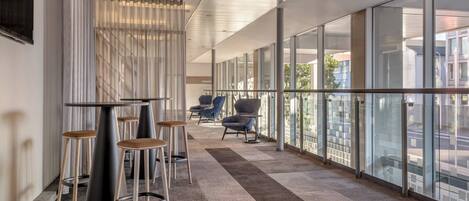 Espaço moderno em ambiente interno com um corredor longo, paredes de vidro e uma variedade de áreas de estar, incluindo banquetas e cadeiras.