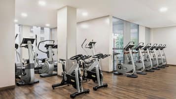 Uma academia com várias bicicletas ergométricas dispostas em fileiras, grandes janelas e piso de madeira.