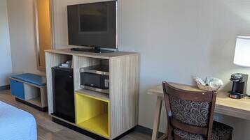 Quarto de hotel com cama, escrivaninha com cadeira, televisão, micro-ondas e cafeteira.