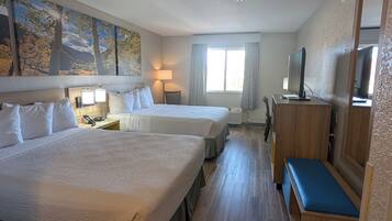 Quarto de hotel com duas camas, uma escrivaninha, uma cadeira, uma televisão e uma janela com cortinas.