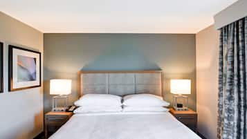 Quarto de hotel com uma cama grande, duas mesas de cabeceira com luminárias, uma cabeceira e um quadro emoldurado na parede.