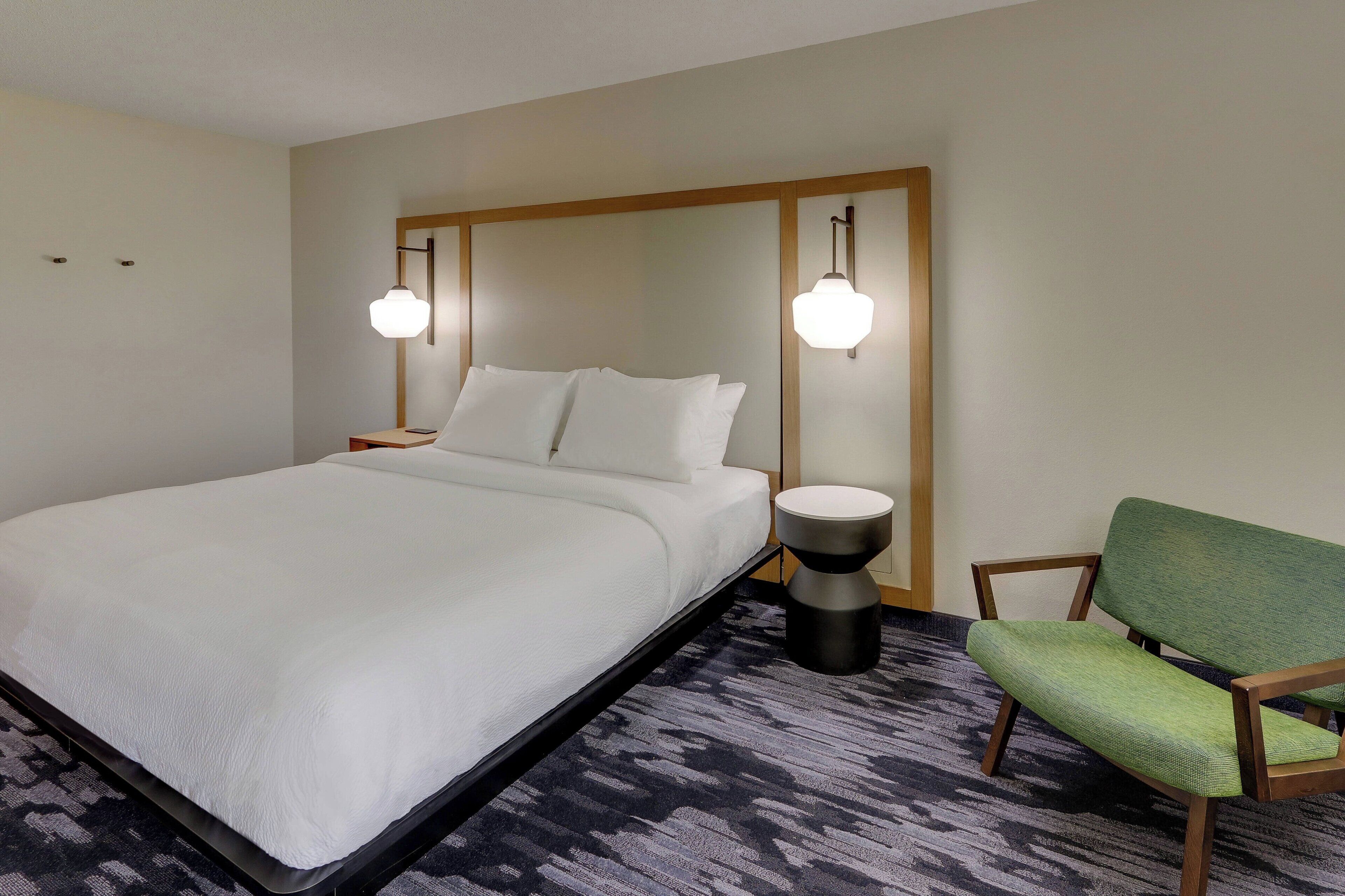 Quarto de hotel com uma cama grande, uma cadeira verde e duas luminárias de cabeceira.