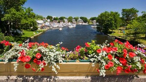 Vista para o rio com barcos atracados, um deck de madeira com flores e casas ao longo da margem.
