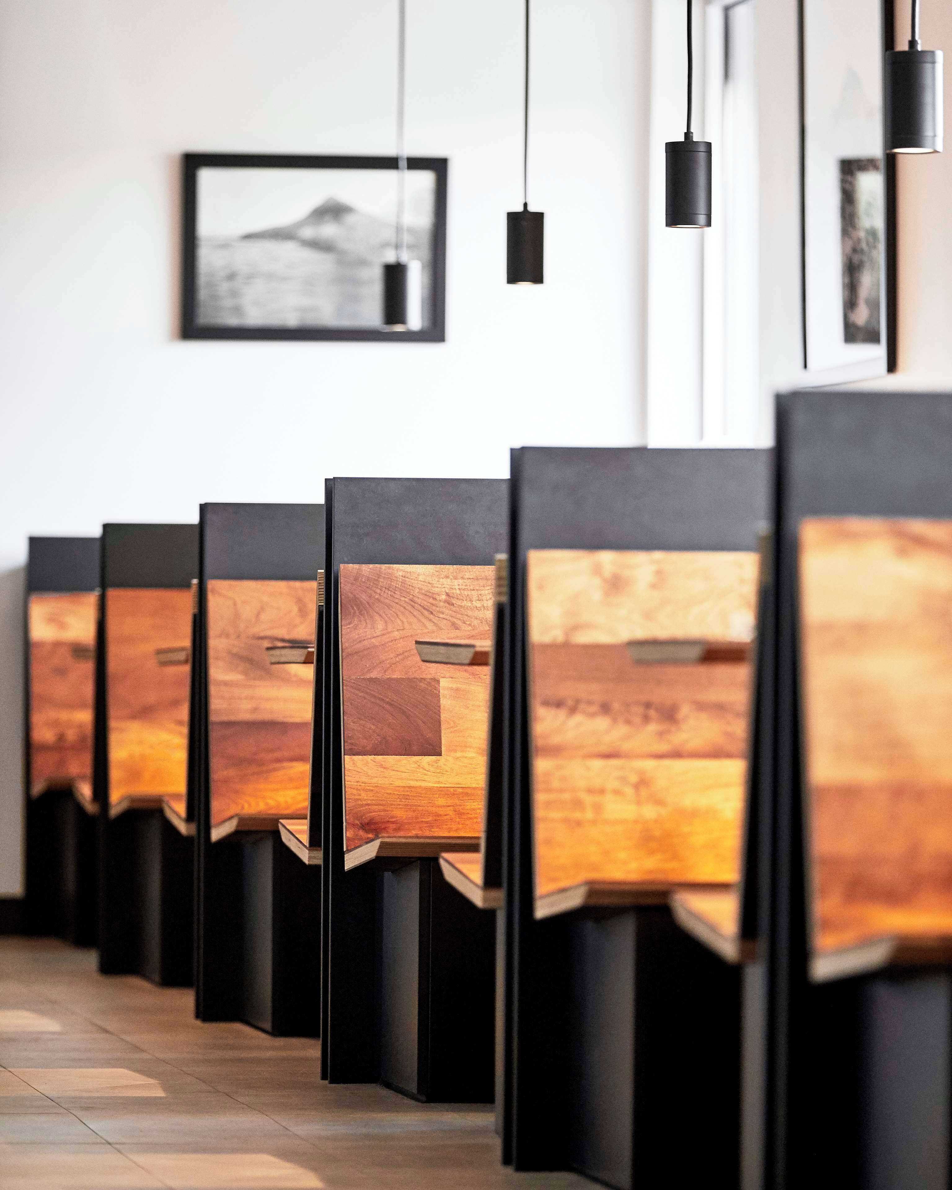 Fileira de armários modernos e minimalistas, com frentes de madeira e bases pretas, dispostos em linha reta contra uma parede branca com um quadro emoldurado acima.