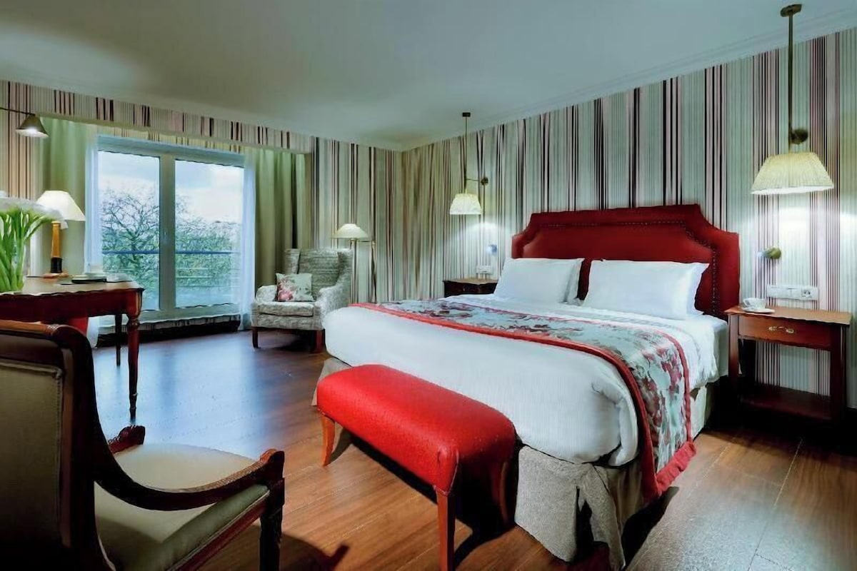 Quarto de hotel com uma cama grande, uma cadeira, uma mesa e vista para o exterior.