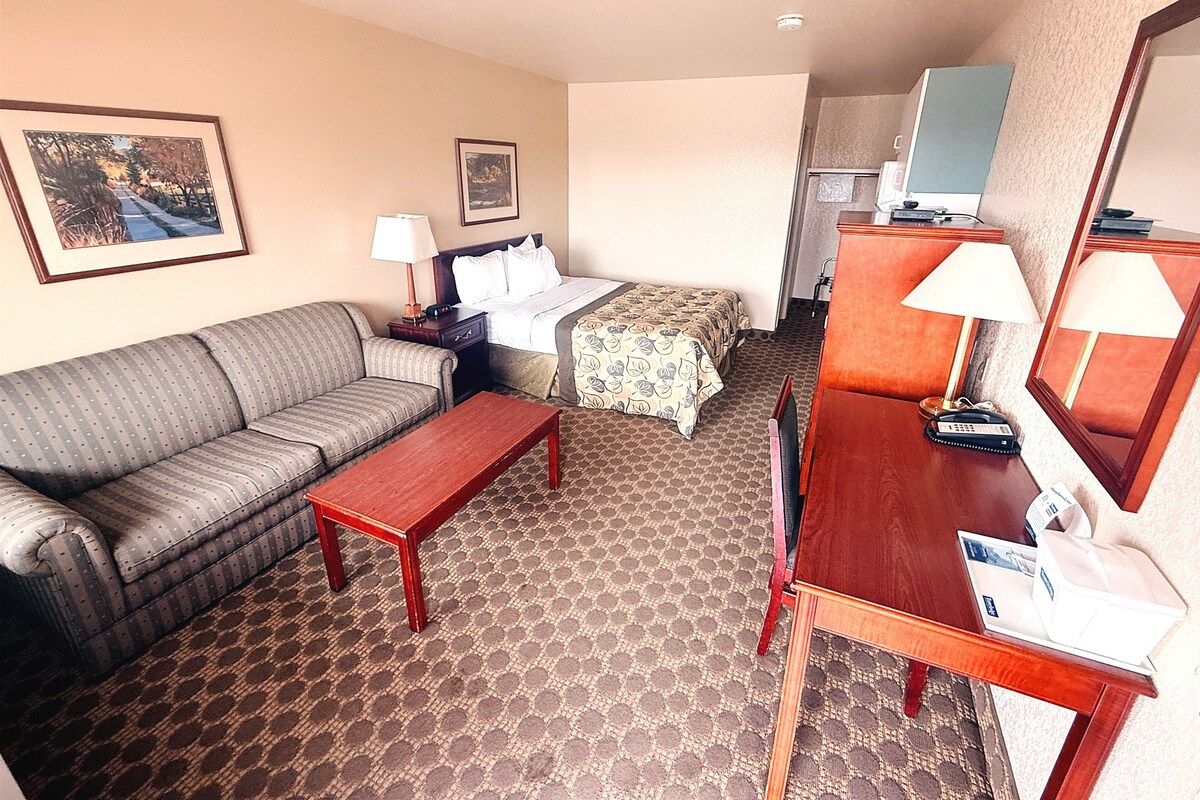 Quarto de hotel com sofá, cama com colcha florida, escrivaninha de madeira e espelho.