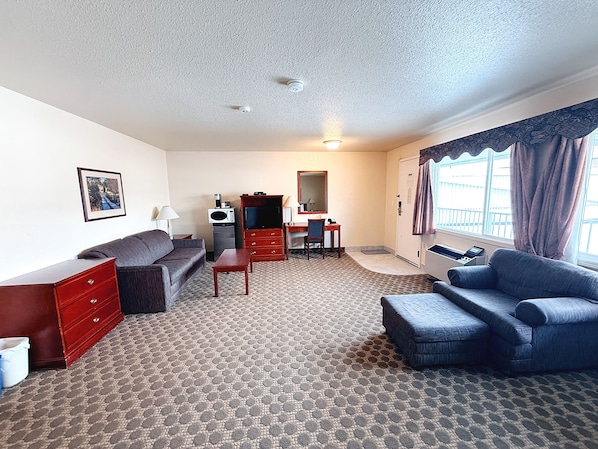 Quarto de hotel com sofá, uma cadeira, secretária com computador, televisão e guarda-roupa.
