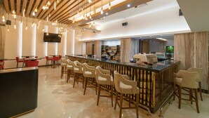 Uma área de bar moderna com um balcão comprido, vários bancos e luminárias pendentes.