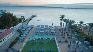 Um hotel à beira-mar com área de piscina, espreguiçadeiras, guarda-sóis e vista para o mar.