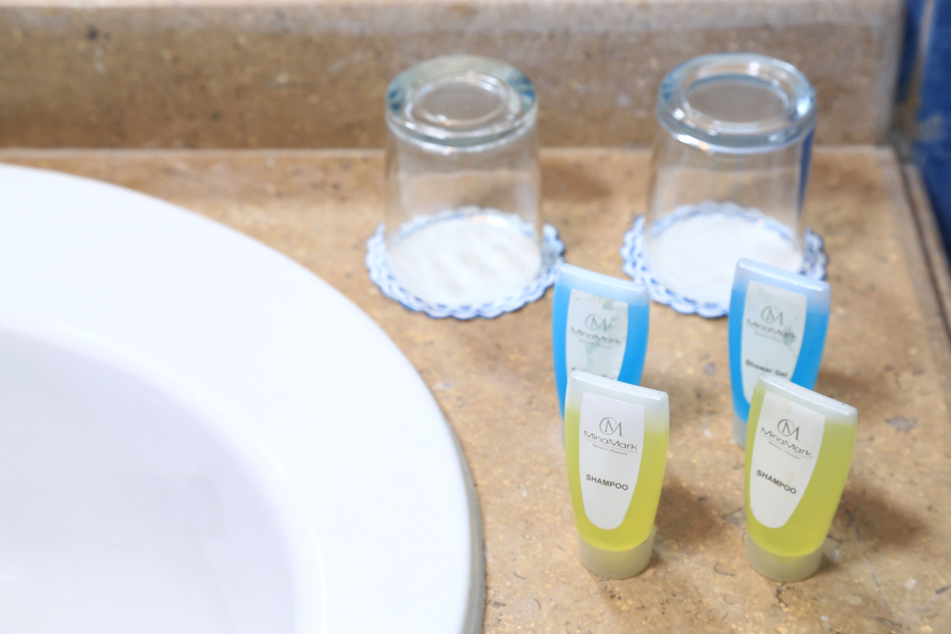 Uma bancada de banheiro com uma pia, dois potes de vidro com tampas e duas pequenas garrafas rotuladas 'MonaMark Shampoo'.