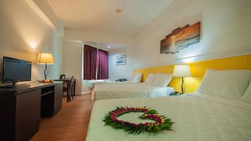 Quarto de hotel com duas camas, uma secretária com televisão e um espaço para refeições.